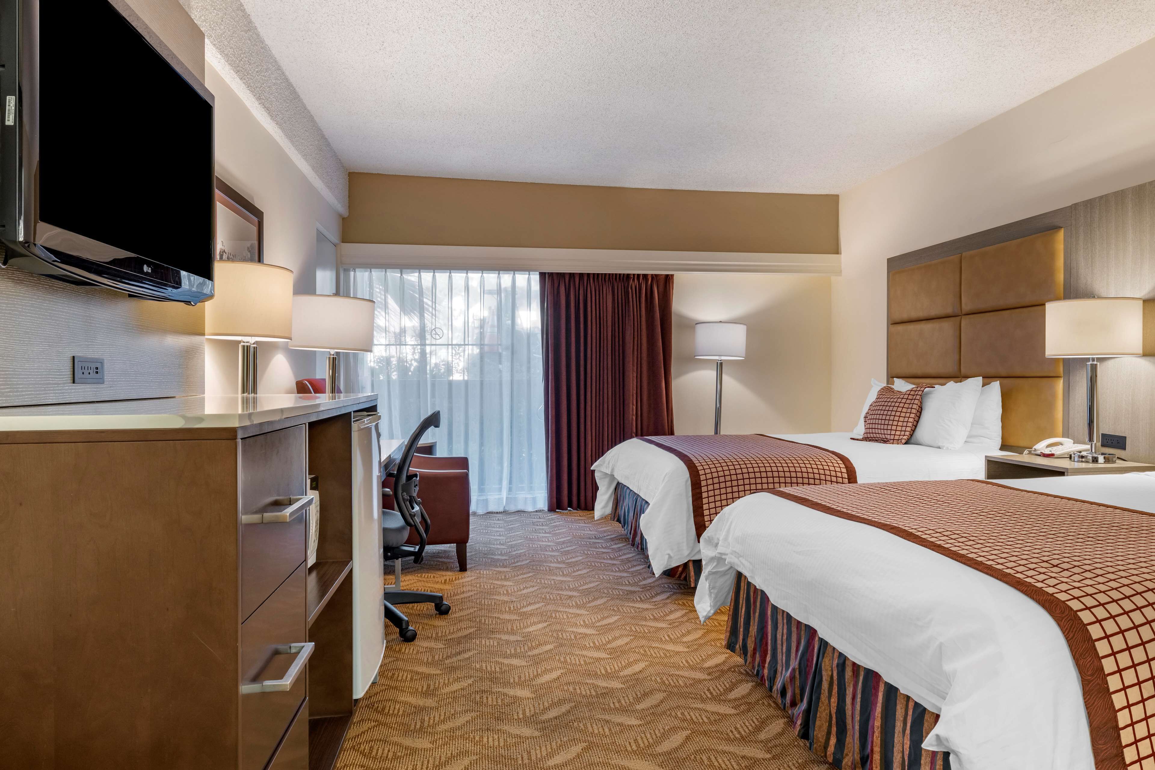 Quarto de hotel com duas camas, televisão, escrivaninha e cadeira.