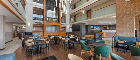Um hall de hotel com vários níveis, átrio central, áreas de estar e balcão de recepção.