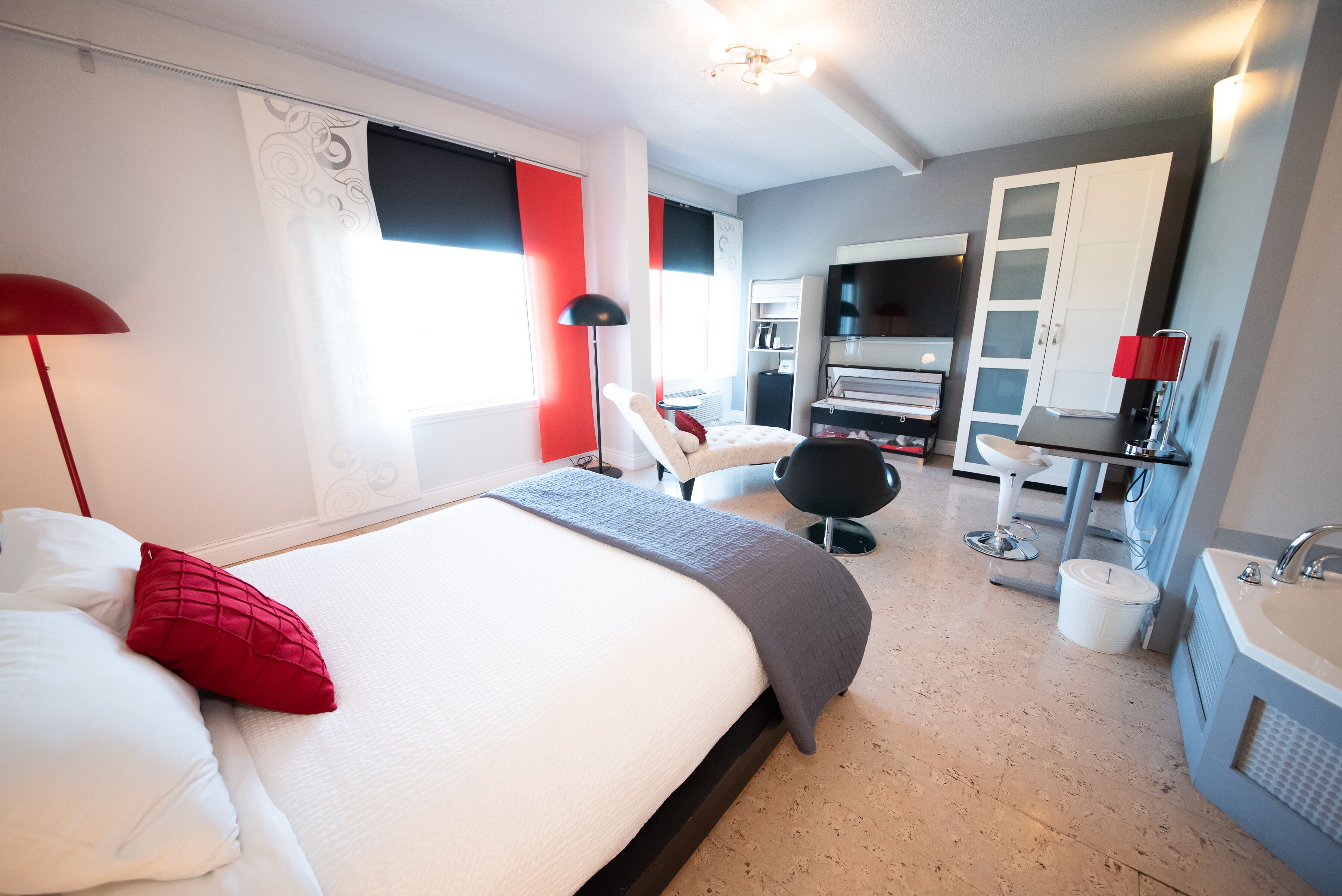 Quarto de hotel moderno com cama, escrivaninha, cadeira, penteadeira e banheiro.