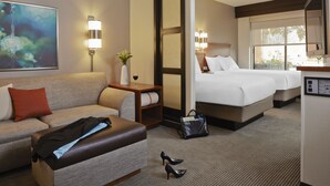 Quarto de hotel com cama, sofá, escrivaninha, espelho e um quadro na parede.