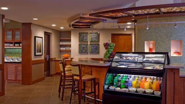 Restaurante com balcão, banquetas, vitrine refrigerada para bebidas e quadros de cardápio.