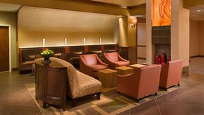 Um lobby com balcão de recepção, área de estar com sofás e poltronas, uma parede decorativa e uma lareira.