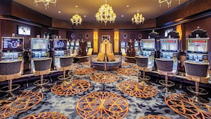 Um cassino com várias máquinas caça-níqueis, banquetas de bar e lustres.