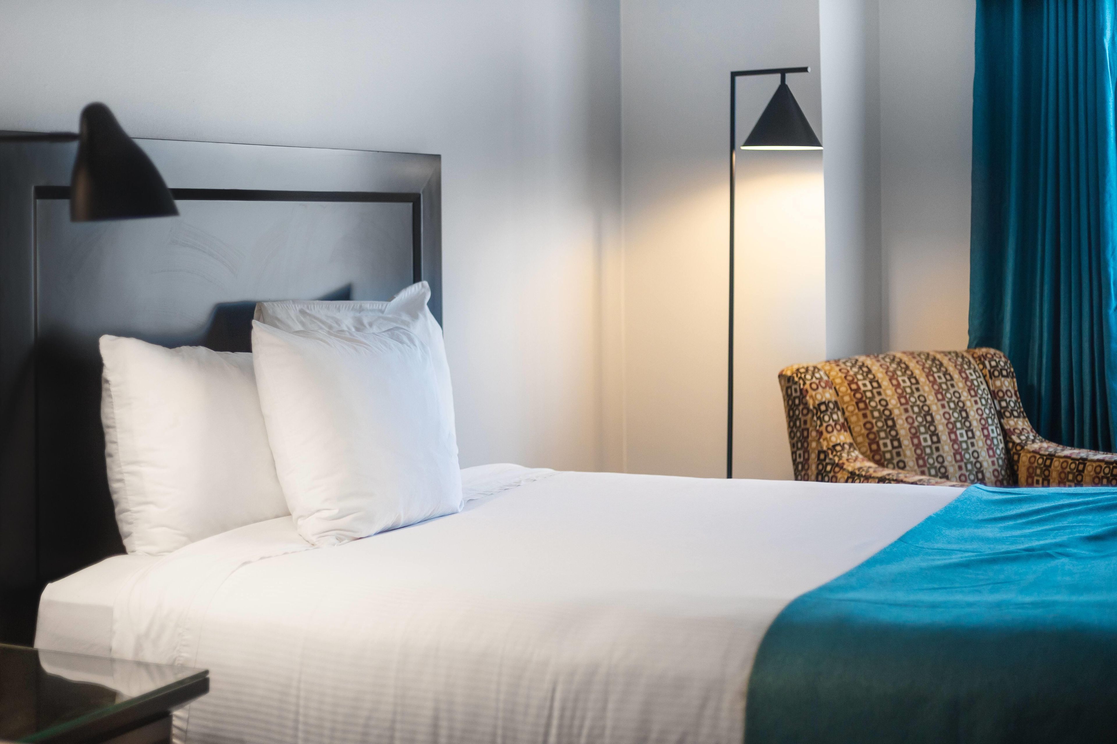 Quarto de hotel com cama, cadeira, mesa de cabeceira e abajur.