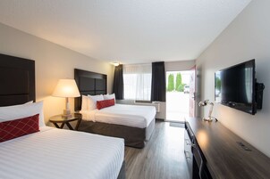 Quarto de hotel com duas camas, televisão, escrivaninha e janela com cortinas.