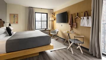 Quarto de hotel moderno com uma cama grande, uma escrivaninha, uma cadeira, uma televisão e vista para a cidade.
