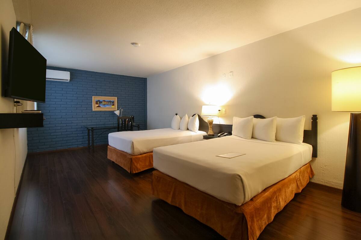 Quarto de hotel com duas camas, televisão, escrivaninha e abajur.