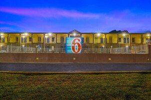 Um motel com um grande letreiro que diz "Motel 6" e uma fileira de quartos com sacadas.