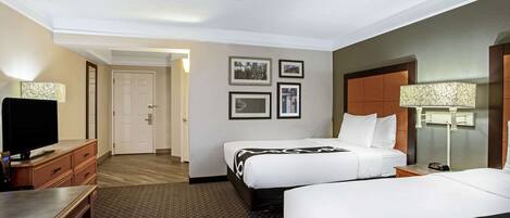 Quarto de hotel com duas camas, uma mesa de trabalho, uma televisão e quadros nas paredes.