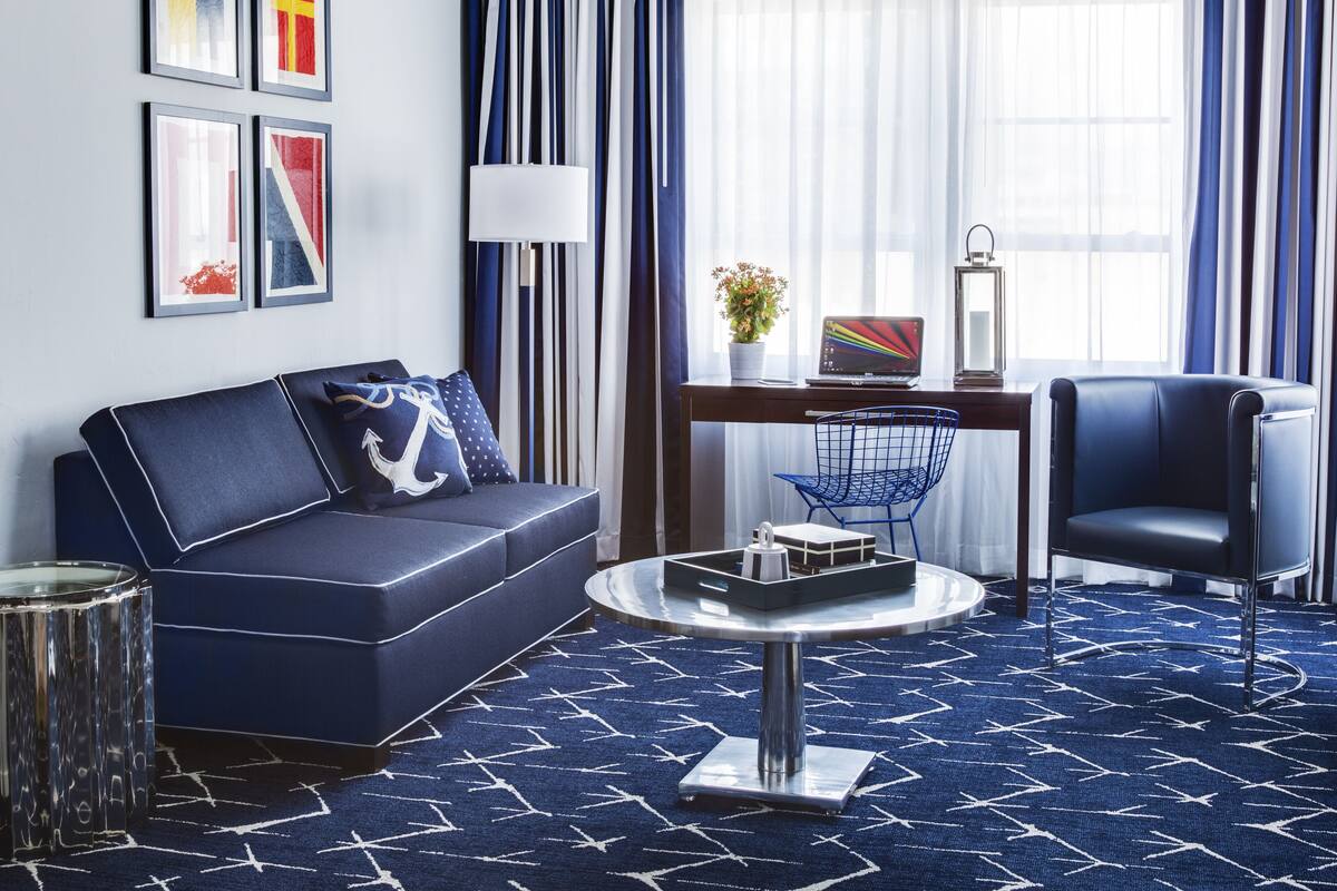 Uma sala de estar moderna com um sofá azul-marinho, uma mesa de centro redonda, uma poltrona azul e uma escrivaninha com um laptop.