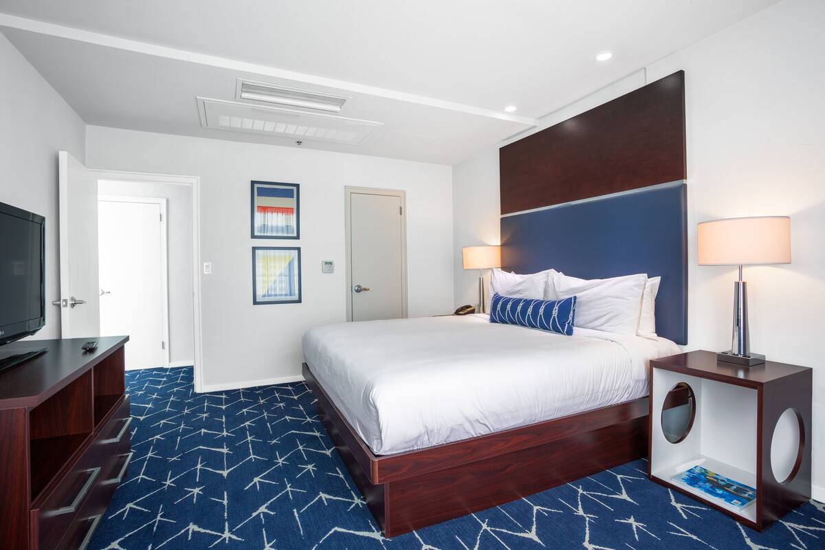 Quarto de hotel com uma cama grande, duas luminárias de cabeceira, uma televisão e um tapete azul estampado.
