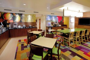Uma área de refeições de hotel com bar, mesas, cadeiras e uma tela grande.