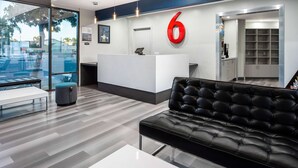 Uma área de recepção moderna com um grande número 6 na parede, um balcão de recepção, um sofá de couro preto e um painel de vidro que dá para o exterior.