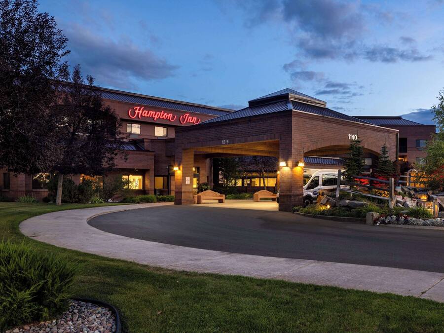 Um hotel Hampton Inn com fachada de tijolos, entrada bem iluminada e canteiro de acesso ajardinado.