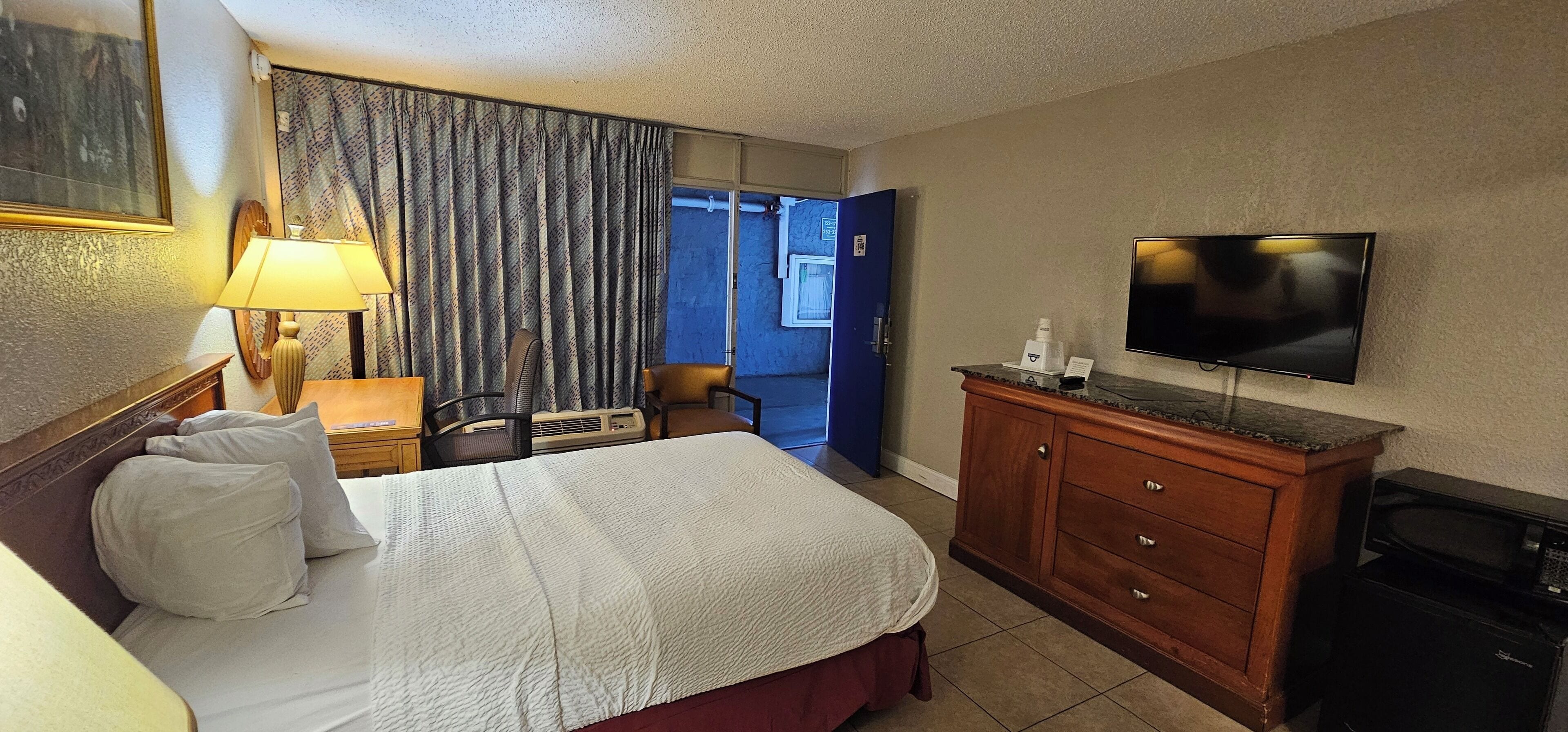 Quarto de hotel com cama, escrivaninha, televisão e micro-ondas.