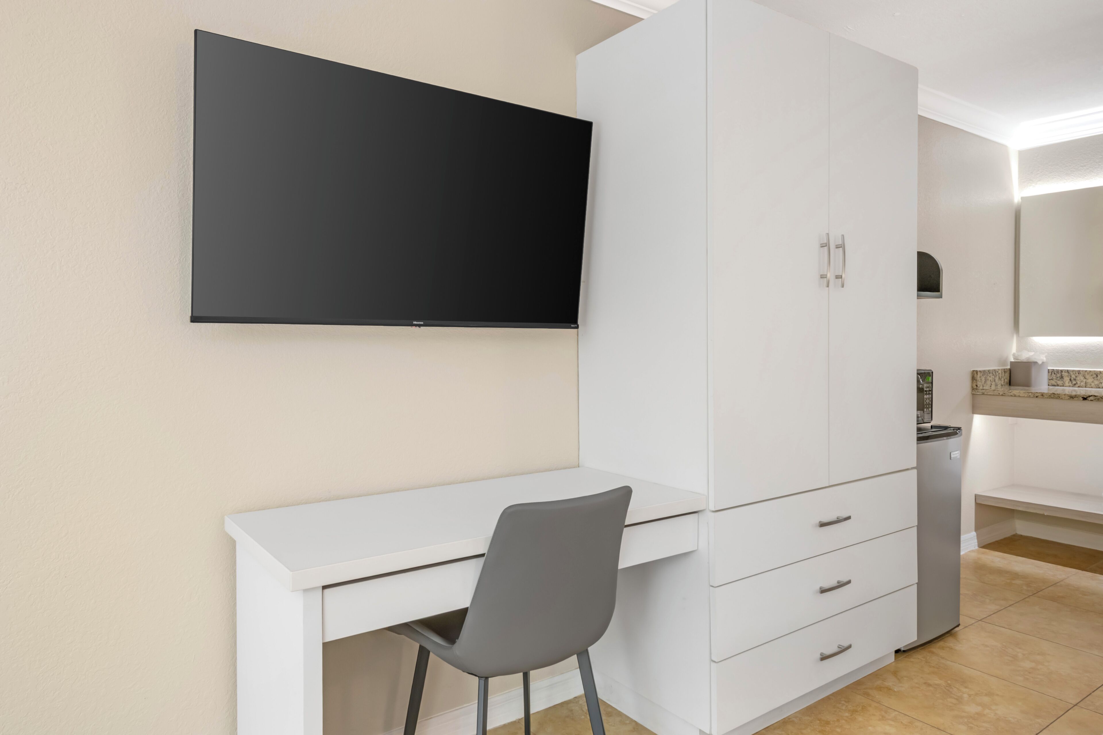 Quarto moderno com escrivaninha branca, cadeira cinza e guarda-roupa espaçoso.