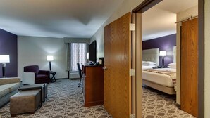 Quarto de hotel com cama, escrivaninha, cadeira, sofá e televisão.