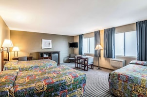 Quarto de hotel com duas camas, uma escrivaninha, uma cadeira, uma televisão e uma janela com cortinas.
