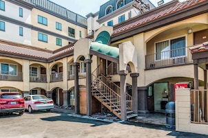 Um hotel com vários andares, uma escadaria espiral central, varandas e um estacionamento com carros.