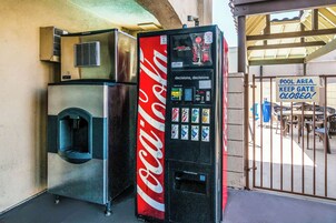 Máquina de refrigerantes Coca-Cola e um frigorífico perto de um portão da área da piscina.