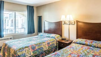 Quarto de hotel com duas camas, uma janela grande com cortinas, mesa de cabeceira com luminárias e vista para edifícios.