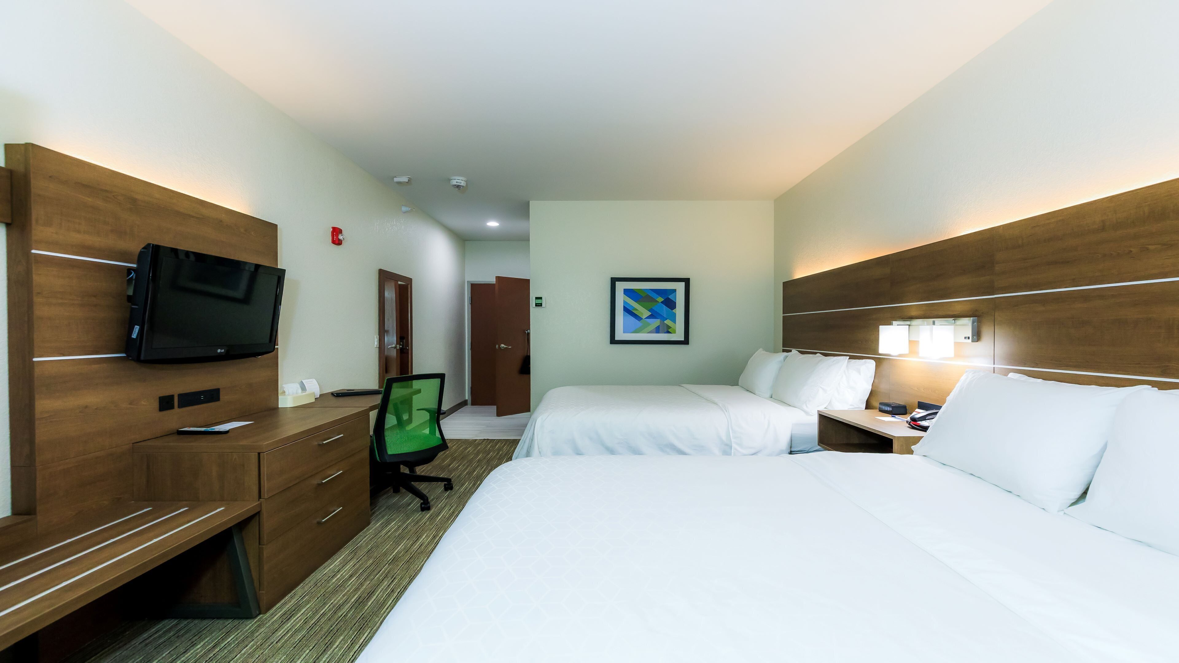 Quarto de hotel com uma cama, uma escrivaninha com computador, uma televisão e uma cadeira.