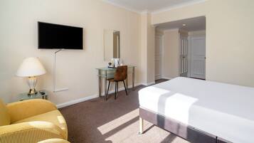 Quarto de hotel com cama, televisão, escrivaninha com cadeira, luminária e sofá.