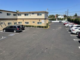 Um estacionamento com vários carros, um edifício com diversas janelas e uma placa indicando limite de velocidade de 8 quilômetros por hora.