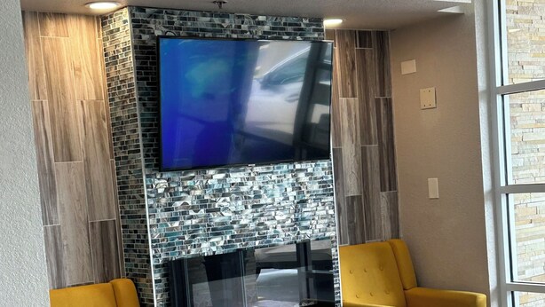 Uma sala de estar moderna com televisão de tela plana, duas poltronas amarelas, uma mesa de centro de madeira e uma parede decorada com padrão de pedra.