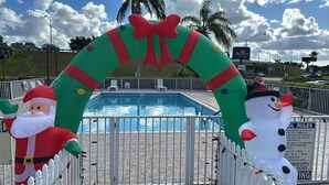 Uma área de piscina com um arco decorativo, Papai Noel e boneco de neve infláveis, e uma placa com as regras da piscina.