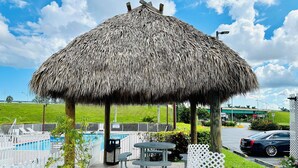 Um gazebo com telhado de palha e área de piscina, incluindo mesa de bilhar e assentos.