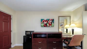 Quarto de hotel com escrivaninha de madeira, uma cadeira, televisão fixada na parede e porta vermelha.