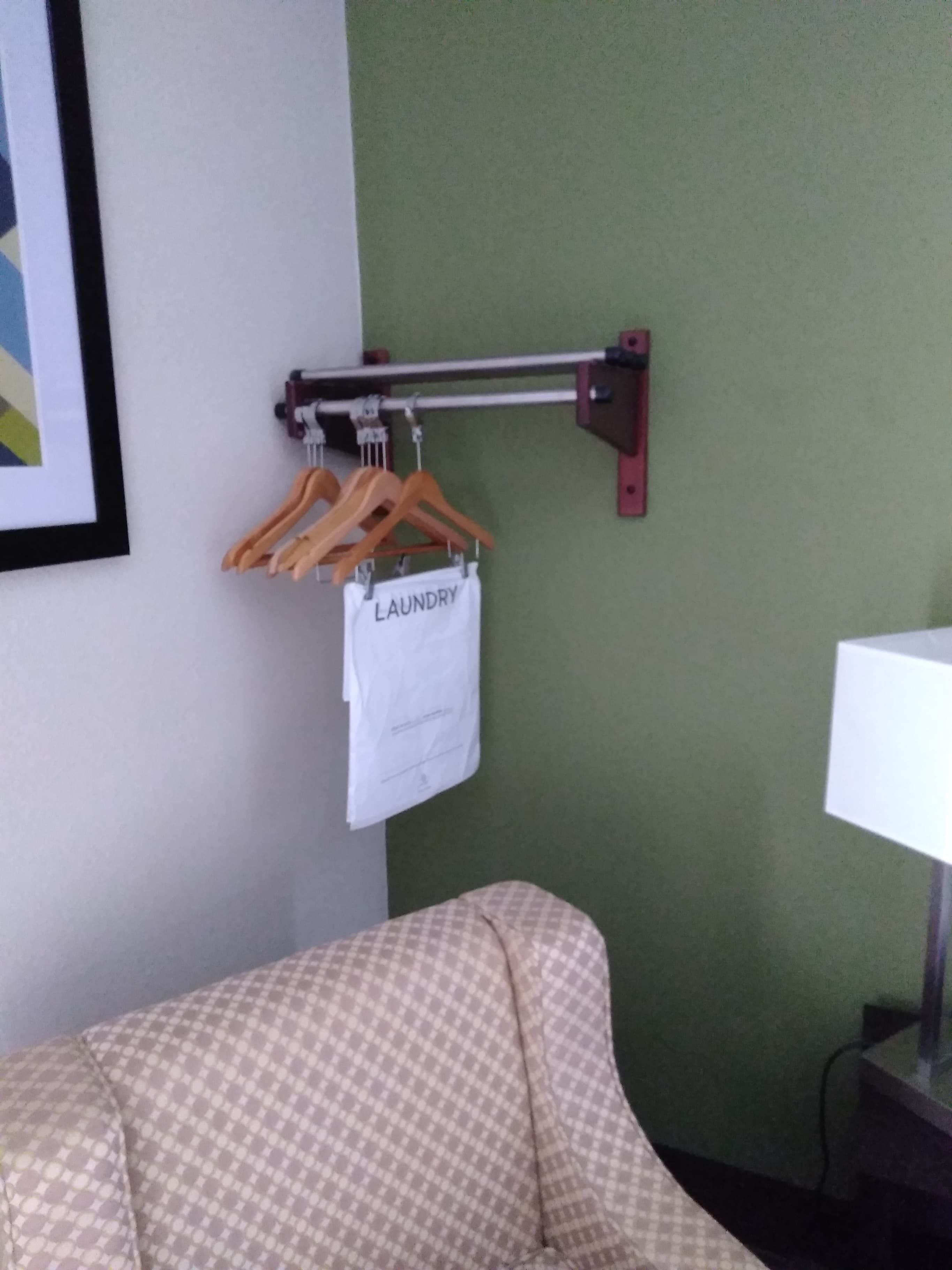 Quarto com parede verde, um quadro emoldurado, um varal com cabides de madeira e um sofá xadrez.