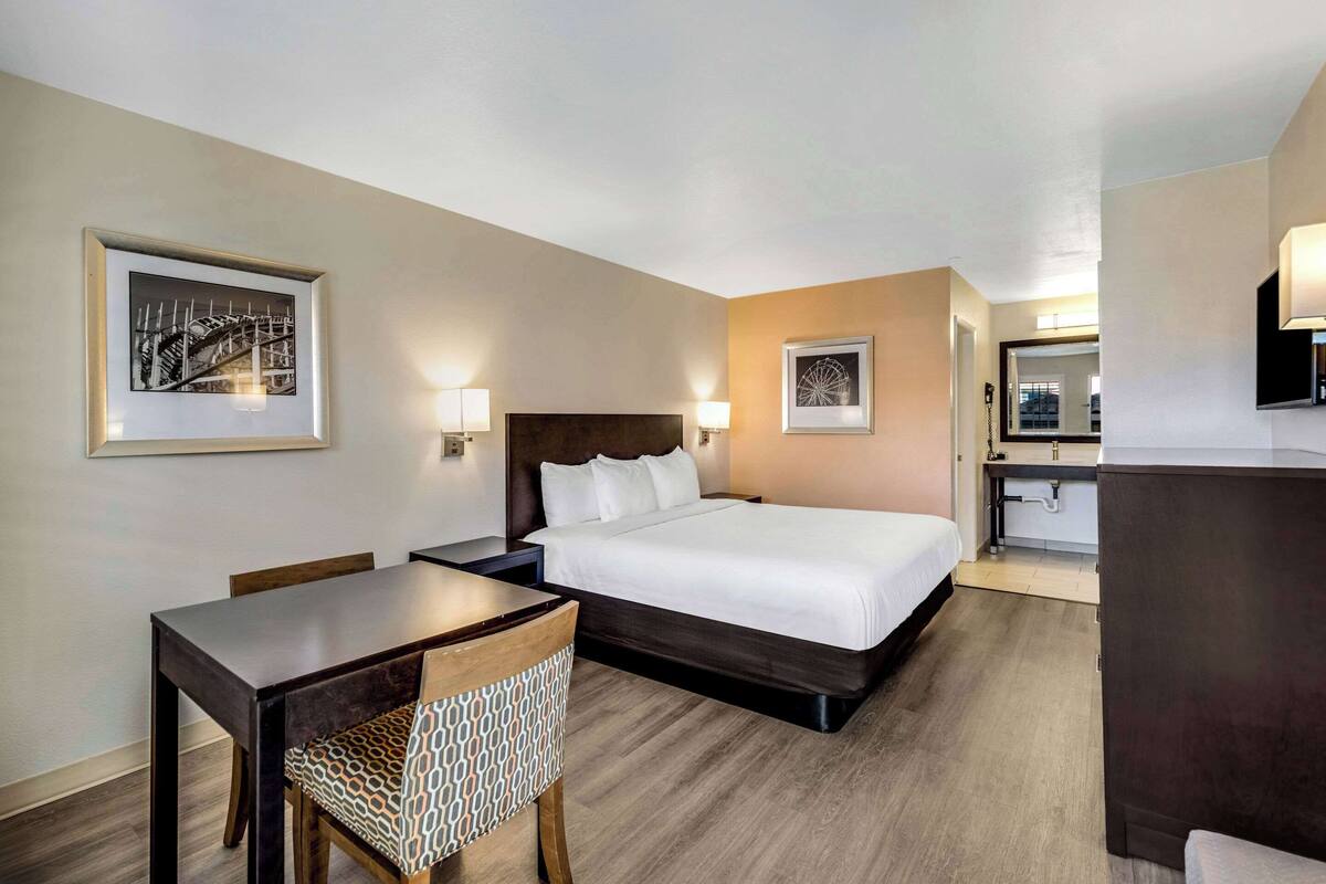 Quarto de hotel com cama, mesas de cabeceira, escrivaninha e cadeiras. Quadros emoldurados adornam as paredes.