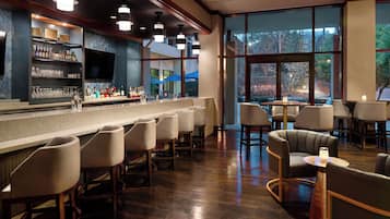 Uma área de bar com um balcão comprido, banquetas e vista para o exterior através de grandes janelas.