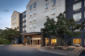 Um hotel de vários andares com design moderno, fachada em pedra, amplas janelas e uma área de entrada bem cuidada com um caminho e paisagismo.