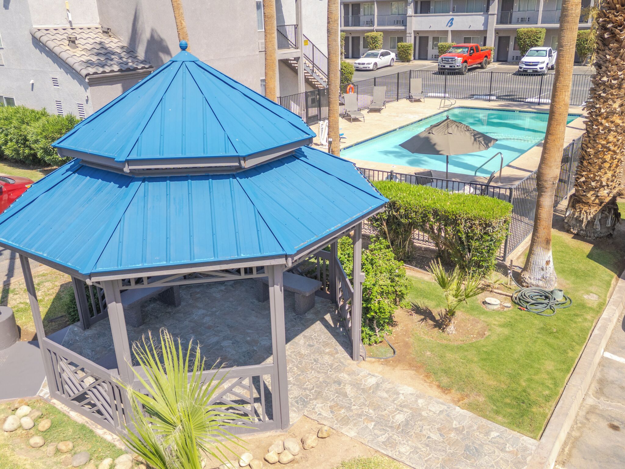 Um gazebo com teto azul, uma piscina e uma área de estacionamento com carros.