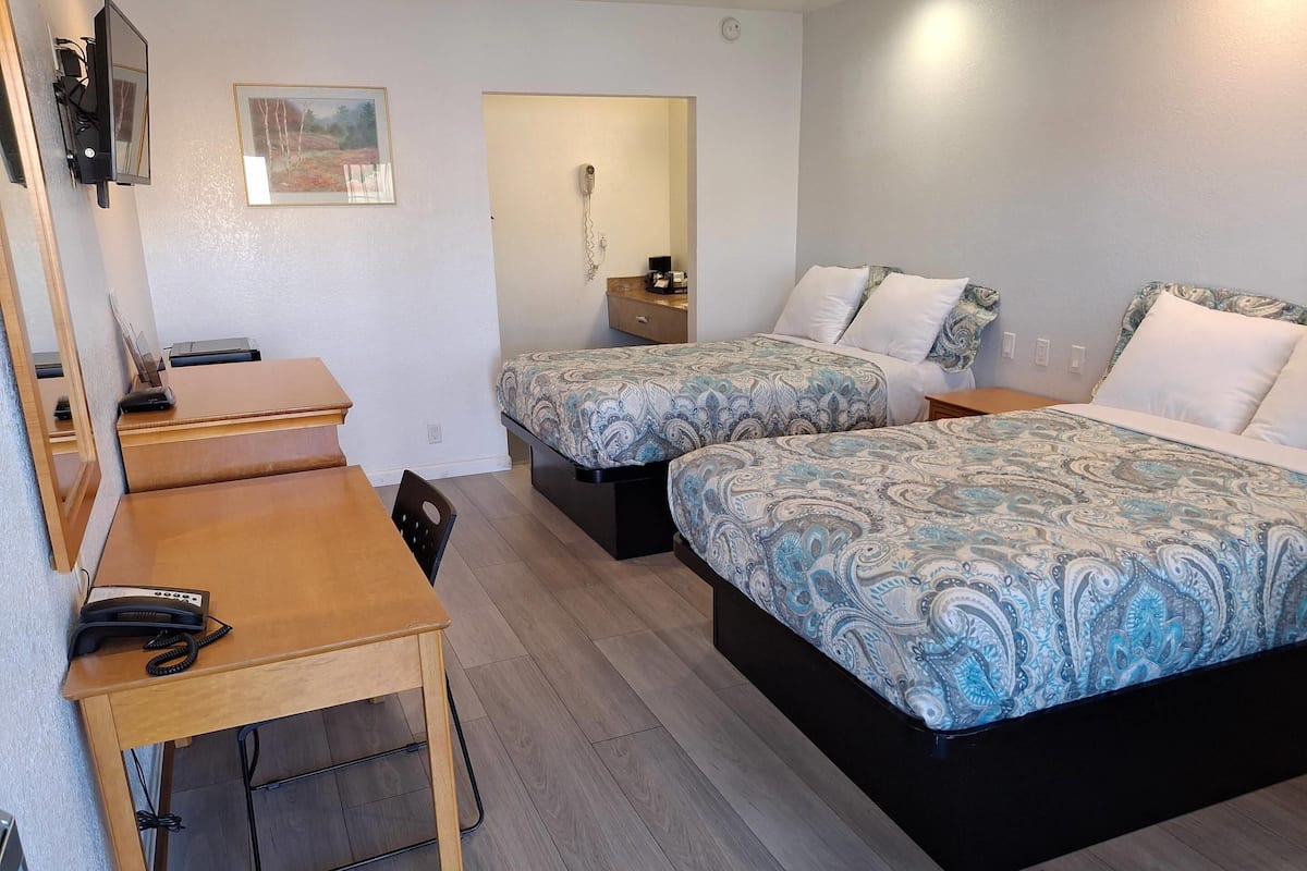 Quarto de hotel com duas camas, uma escrivaninha, uma cadeira, um telefone e uma mesinha.
