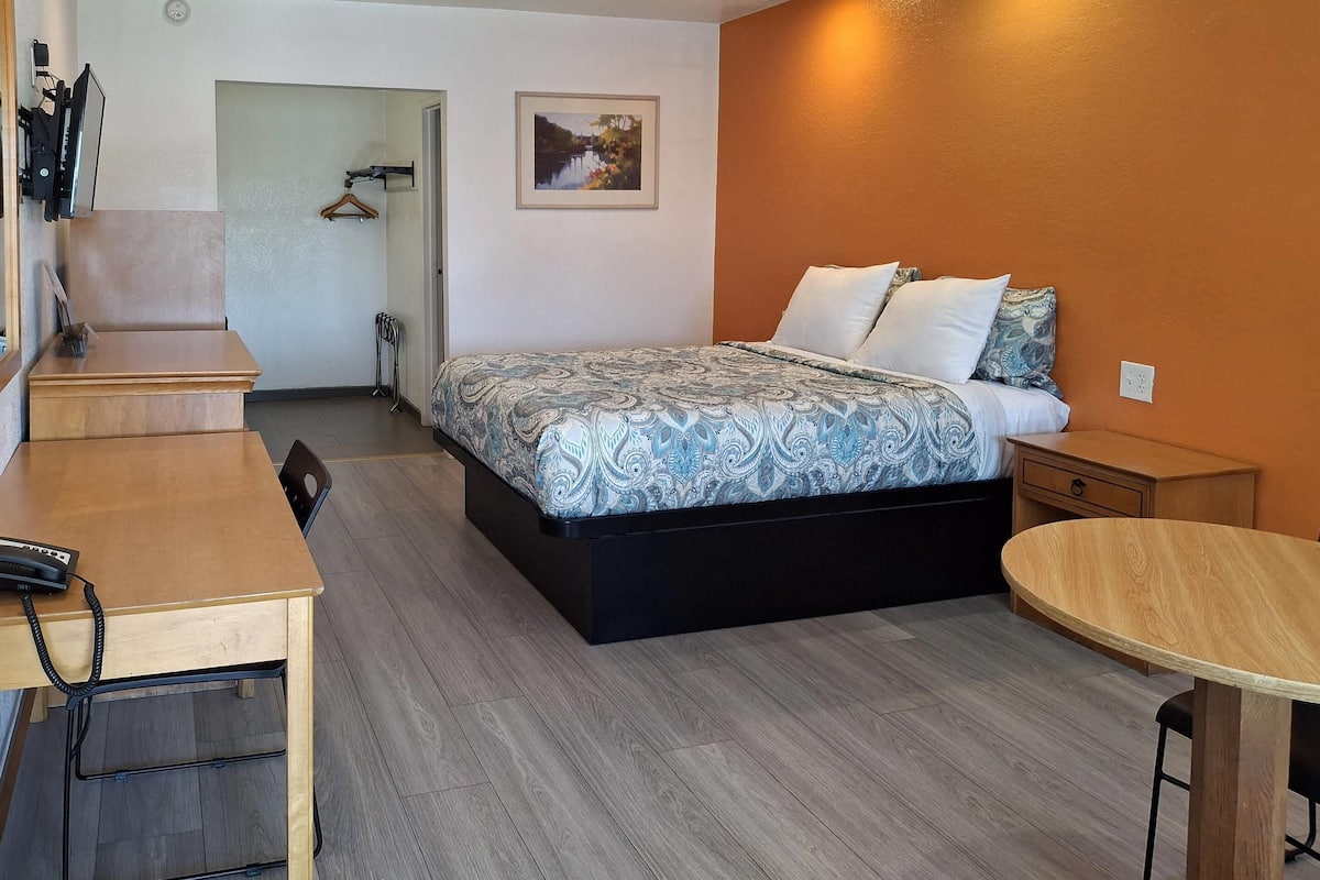 Quarto de hotel com cama, escrivaninha, cadeira e uma mesinha.