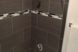 Chuveiro com azulejos escuros e ralo aparente.