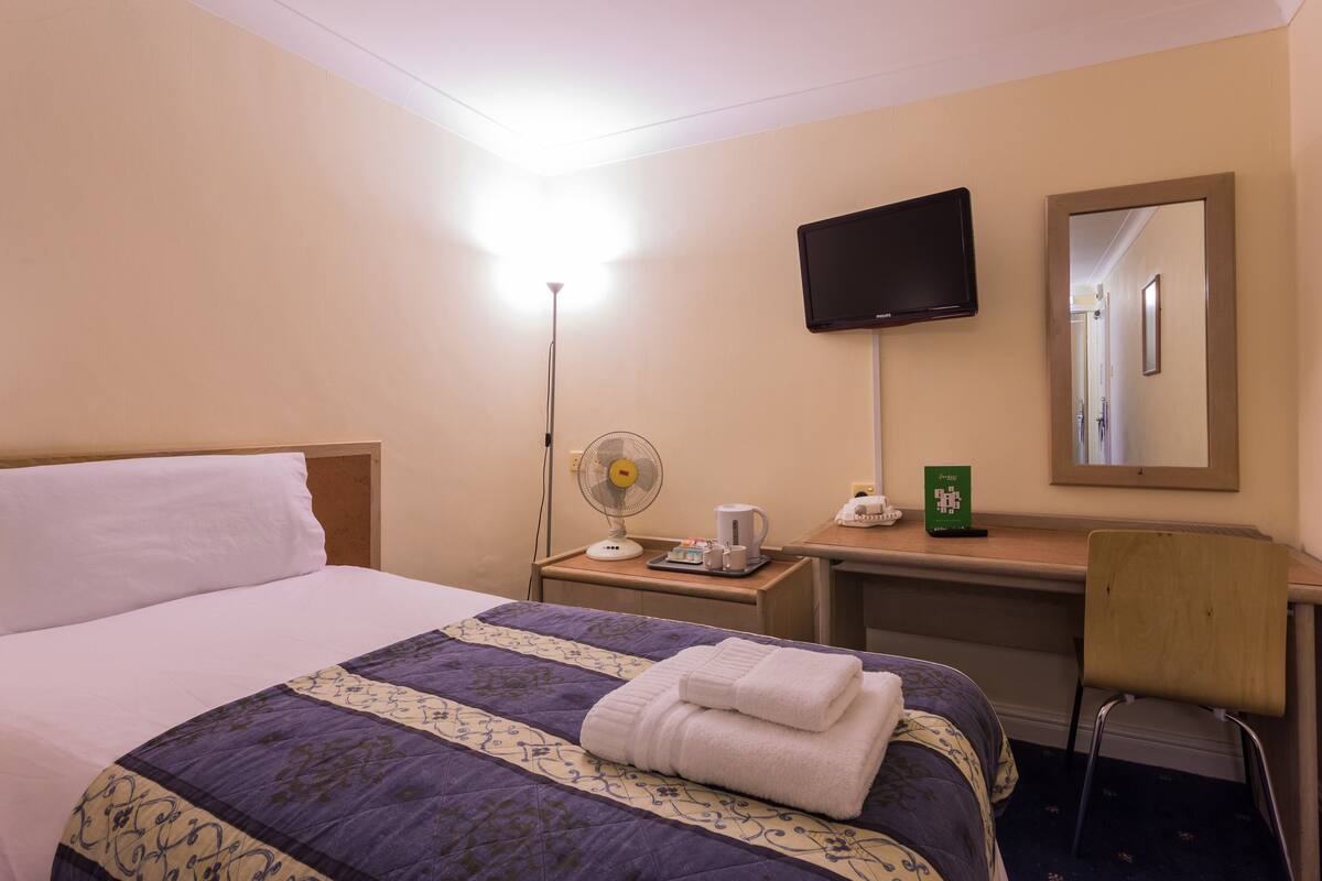 Quarto de hotel com cama, secretária, televisão de ecrã plano, ventoinha e cadeira.