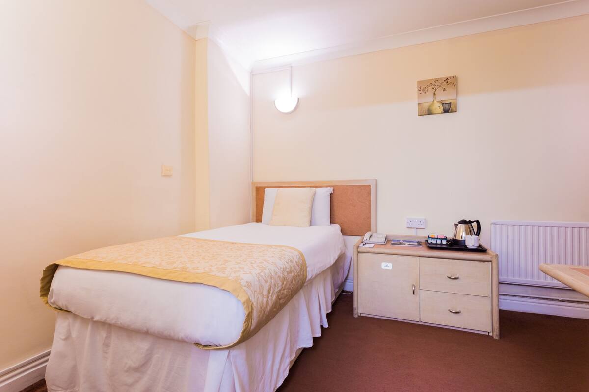 Quarto de hotel com cama, mesa de cabeceira e um pequeno armário.