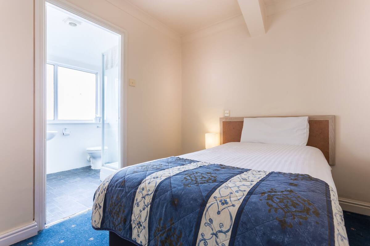 Quarto de hotel com cama, abajur e vista para o banheiro.