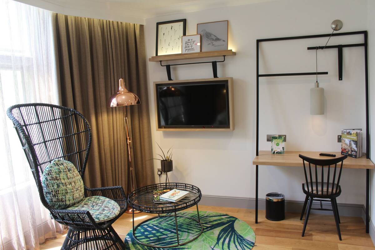 Uma sala de estar moderna com uma cadeira de arame preta, uma mesa de centro redonda, uma televisão e uma escrivaninha com uma cadeira.