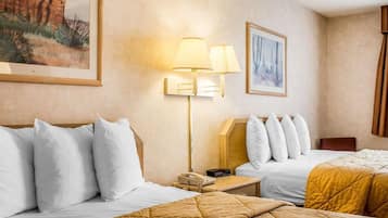 Quarto de hotel com duas camas, uma mesinha de cabeceira com abajur, um quadro na parede e uma janela com cortinas.
