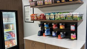 Espaço de lanches e bebidas com serviço próprio, com produtos refrigerados e prateleiras repletas de diversas opções de lanches e bebidas.