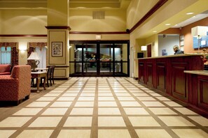 Um saguão de hotel com balcão de recepção, área de estar e piso ladrilhado.