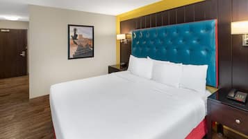 Quarto de hotel com uma cama grande, mesa de cabeceira com telefone, luminária na parede e um quadro emoldurado.