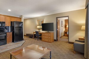 Quarto de hotel compacto com cozinha compacta, televisão de tela plana, escrivaninha e área de estar.