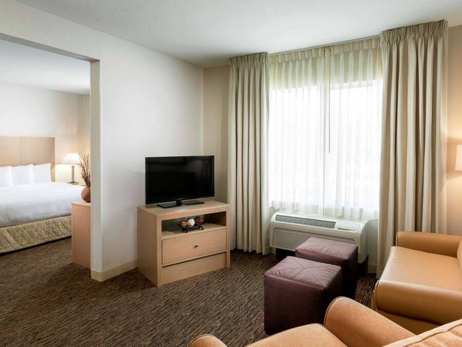 Quarto de hotel com cama, televisão, sofá e janela com cortinas.